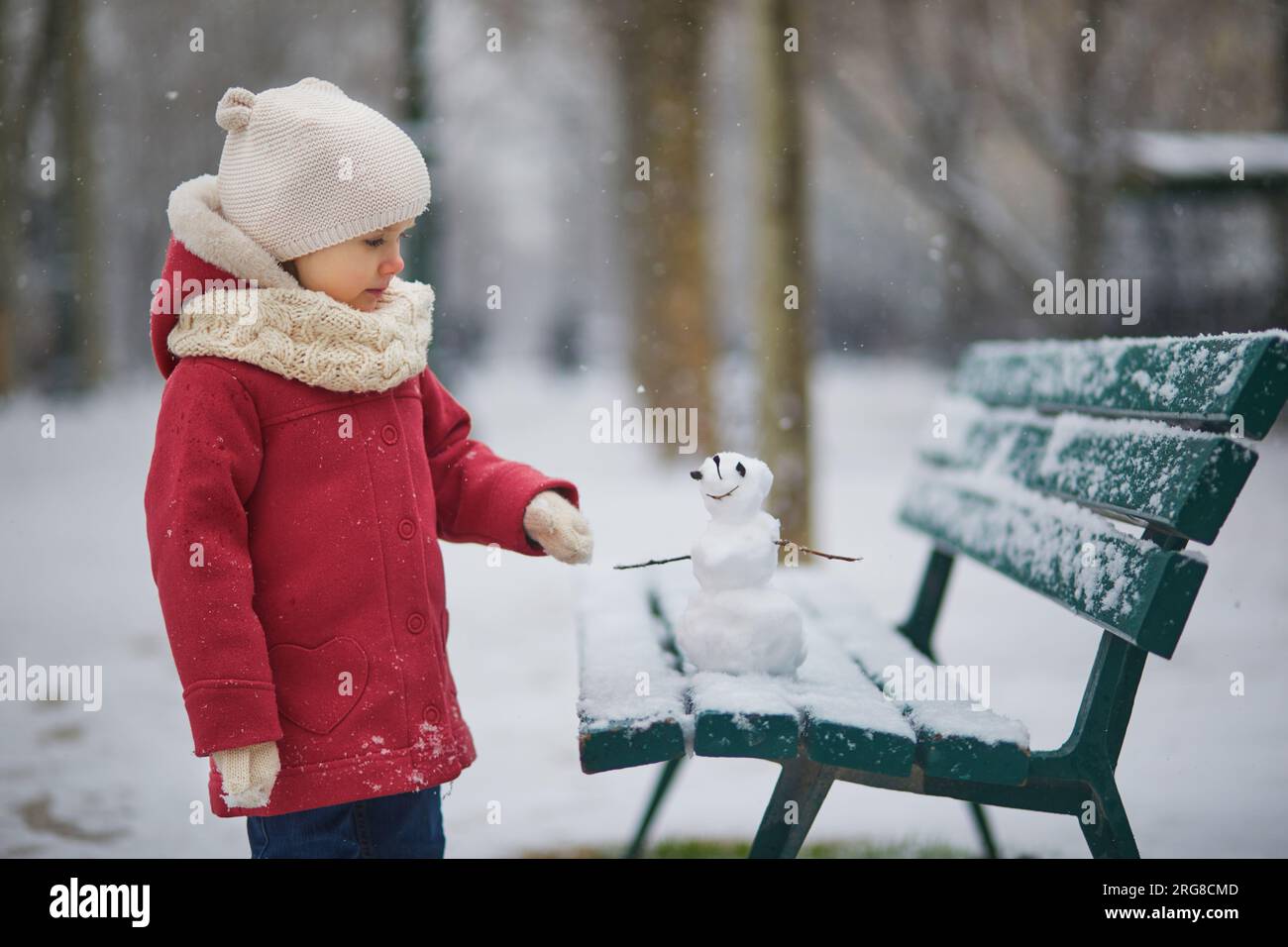 Adorable toddler girl building a snowman on a day with heavy snowfall ...