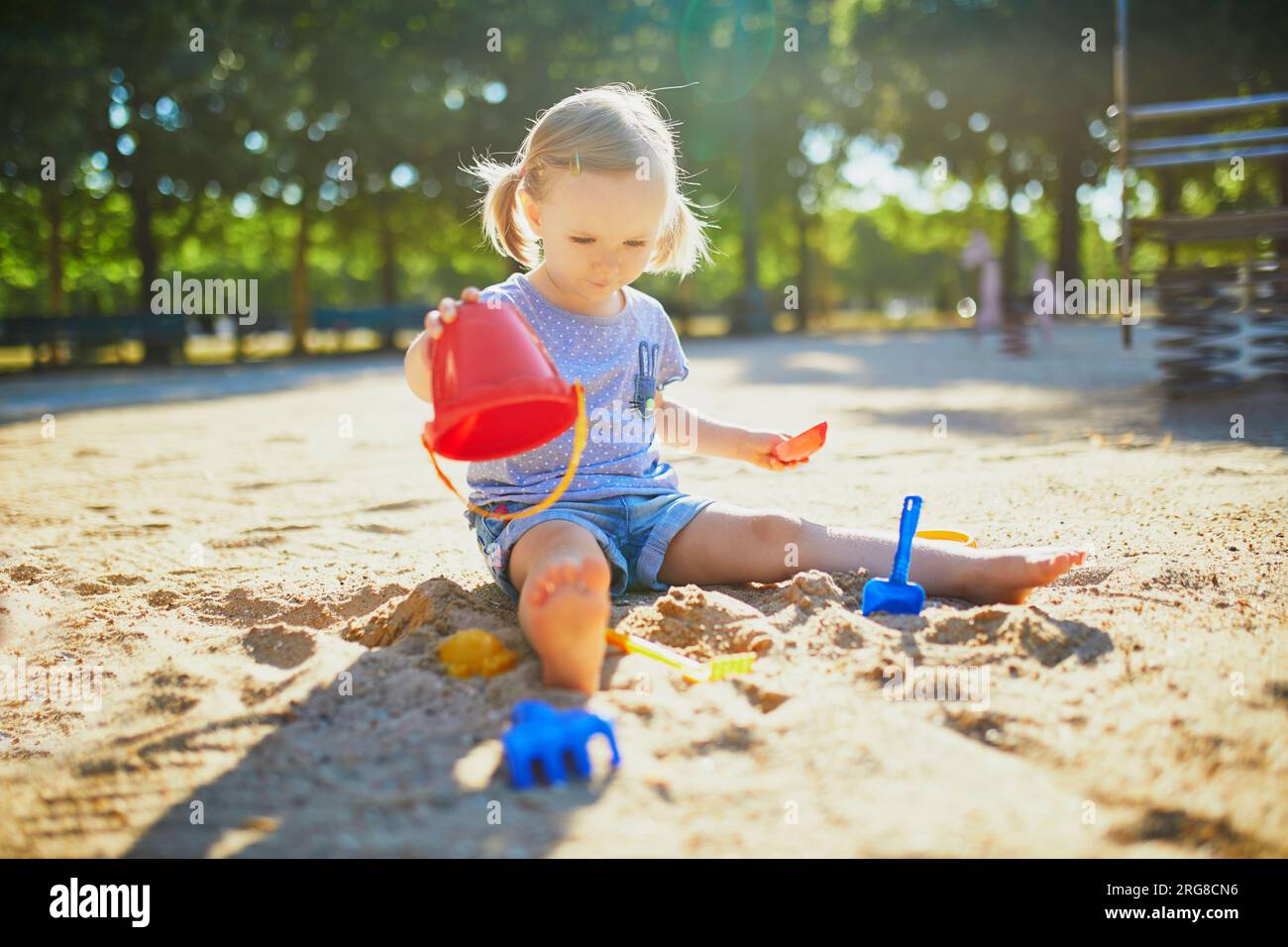 Adorable little girl having fun on playground in sandpit. Toddler playing with sand molds and ...