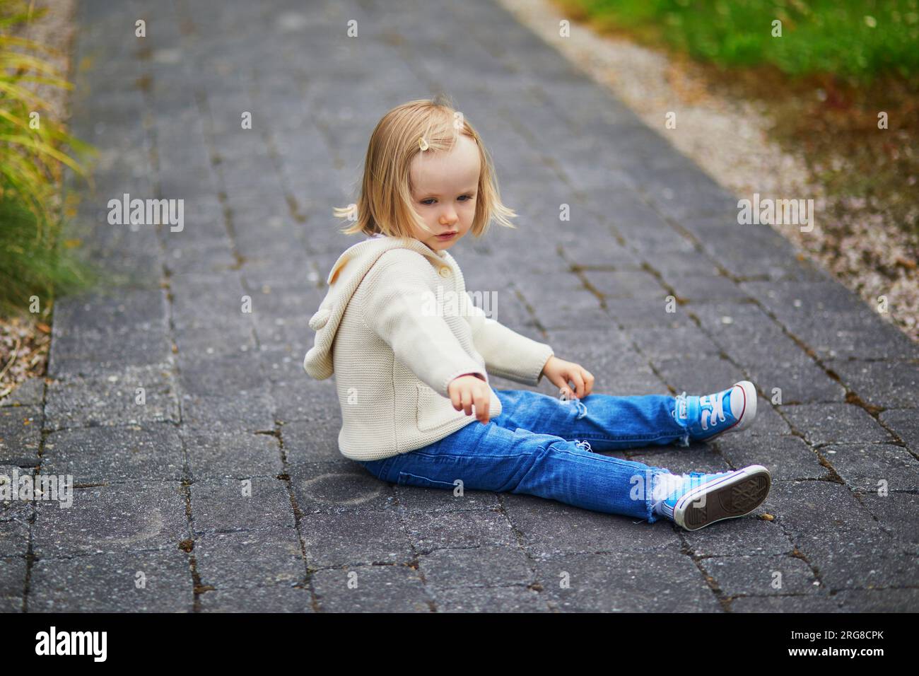 Unhappy and emotional toddler girl sitting on the floor outdoors ...