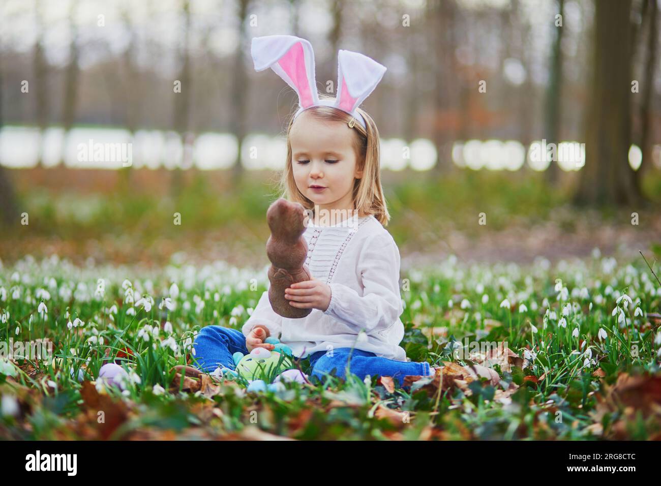 Girl wearing bunny ears playing egg hunt on Easter. Toddler sitting on ...