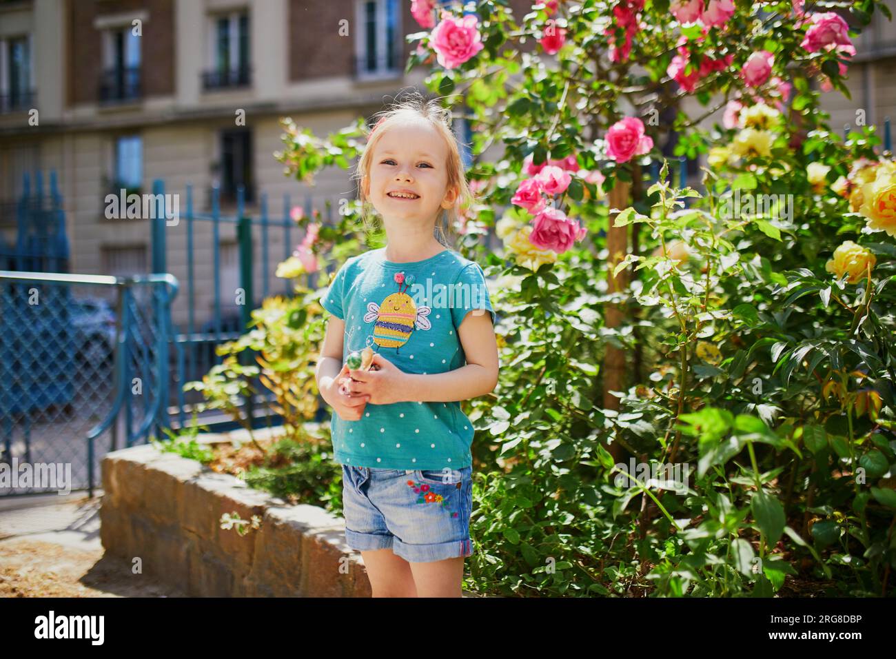 Adorable preschooler girl enjoying rose flowers in summer park. Happy ...