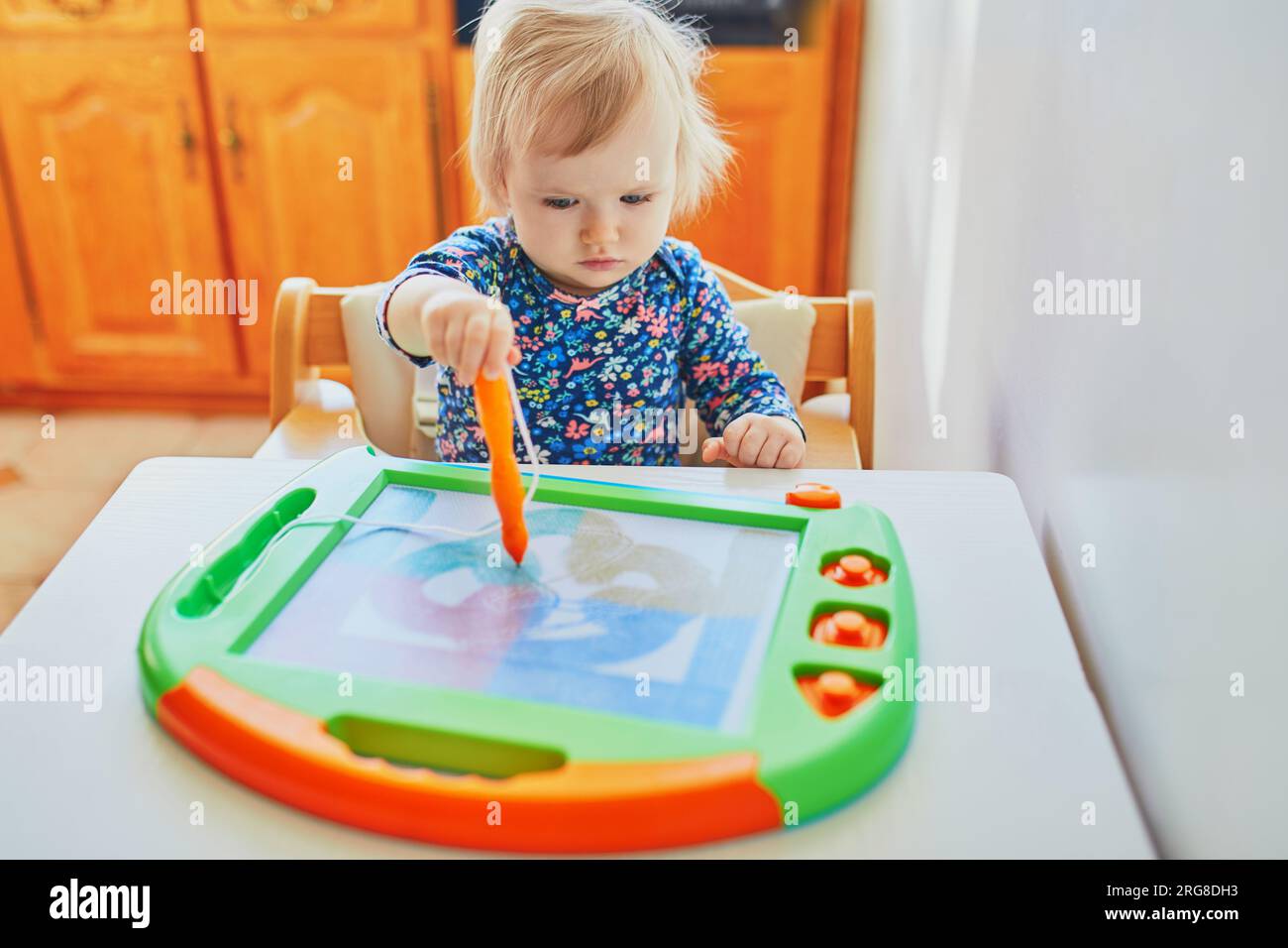 Adorable little girl drawing on magnetic magic screen at home, in ...