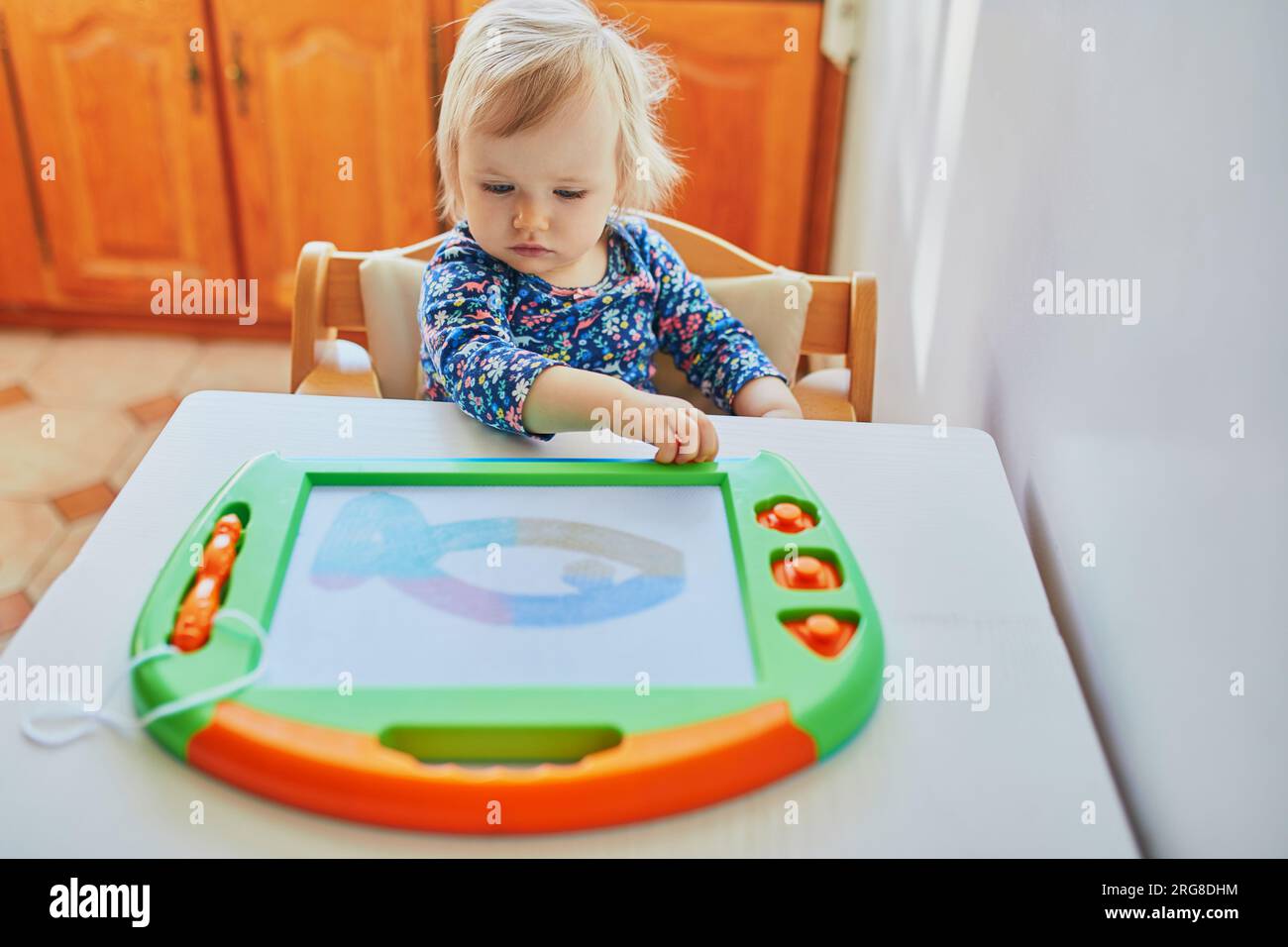Adorable little girl drawing on magnetic magic screen at home, in ...