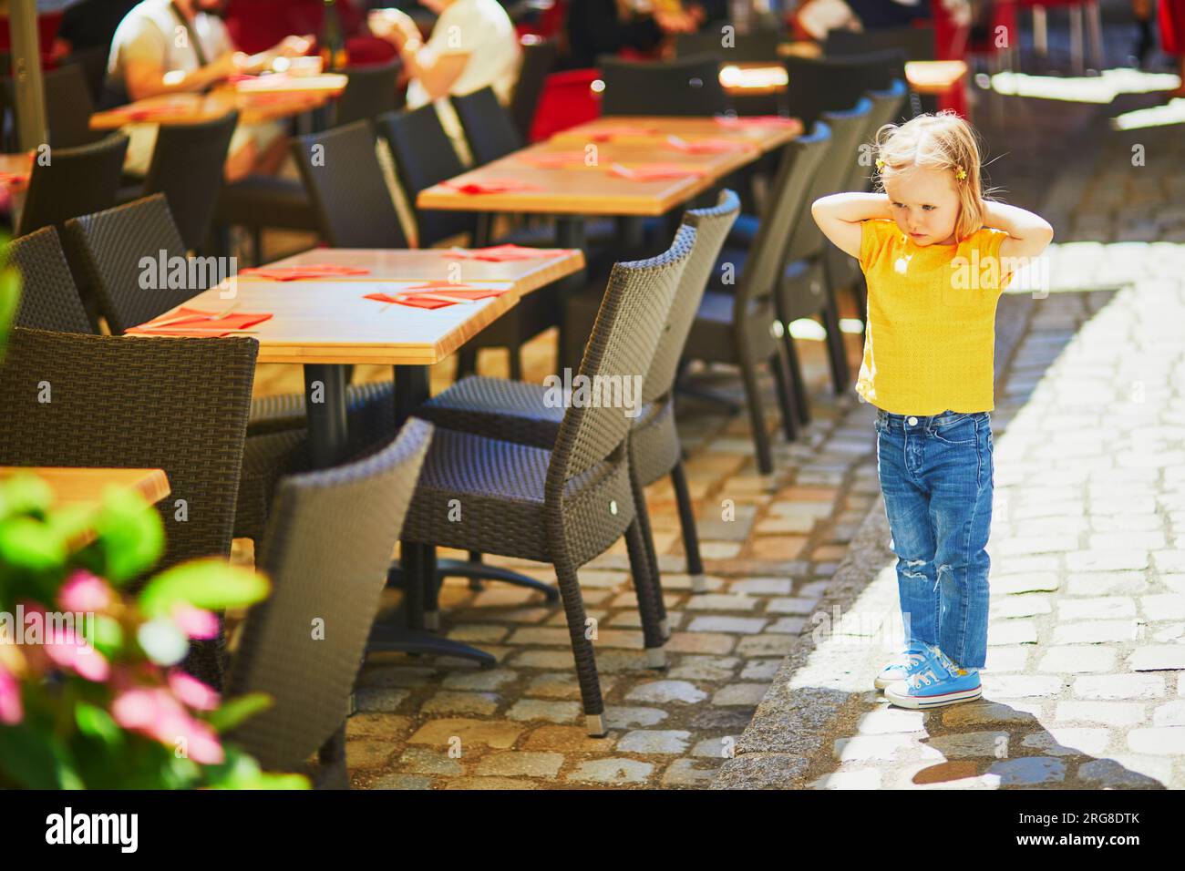 Unhappy and stubborn toddler girl in outdoor restaurant. Misbehaving ...