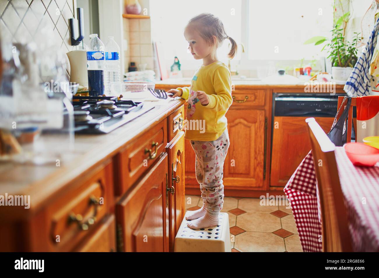 Adorable toddler girl cooking in the kitchen at home, helping to ...