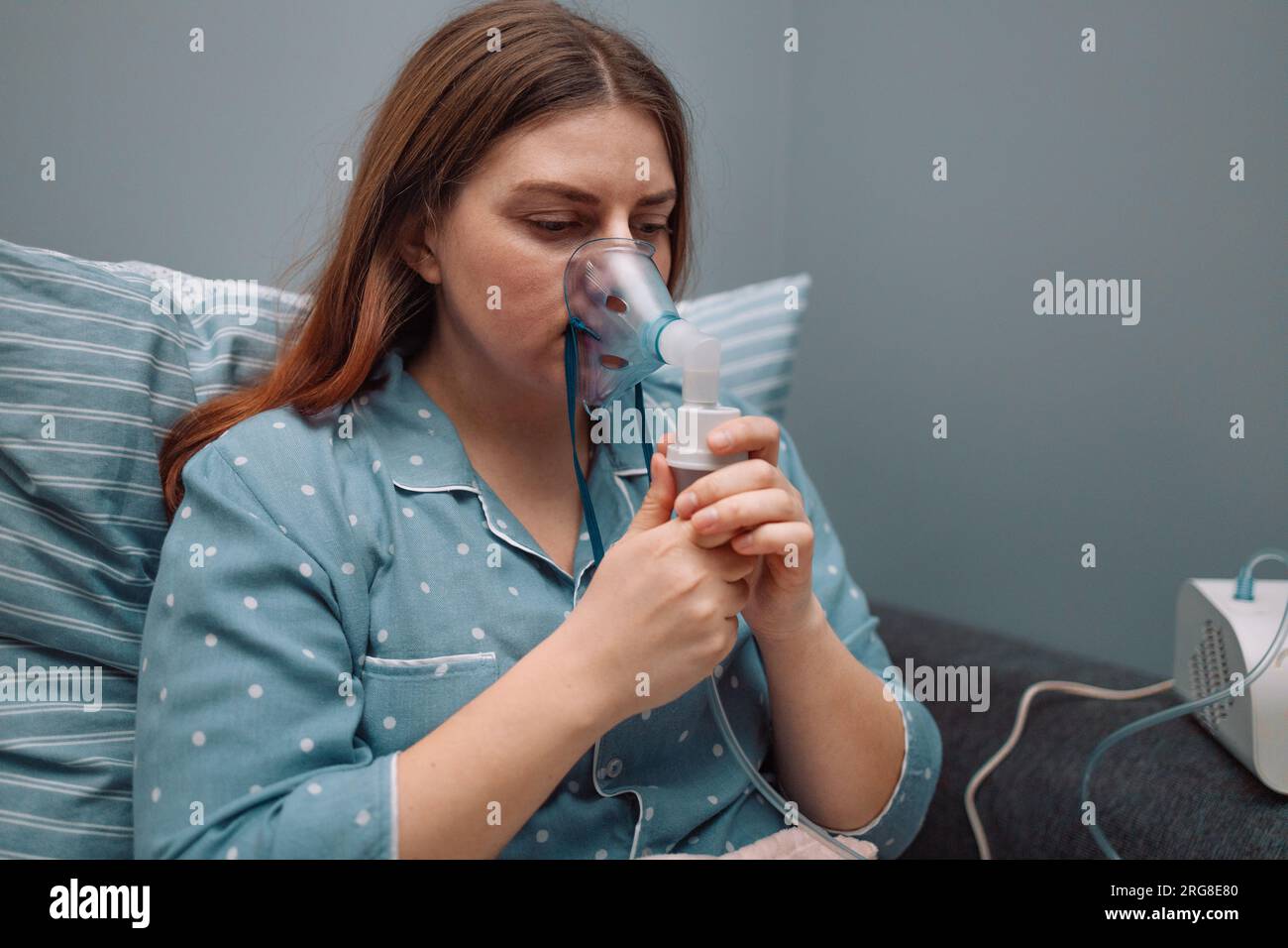 Young sick woman putting on nebulizer mask on face to make inhalation ...