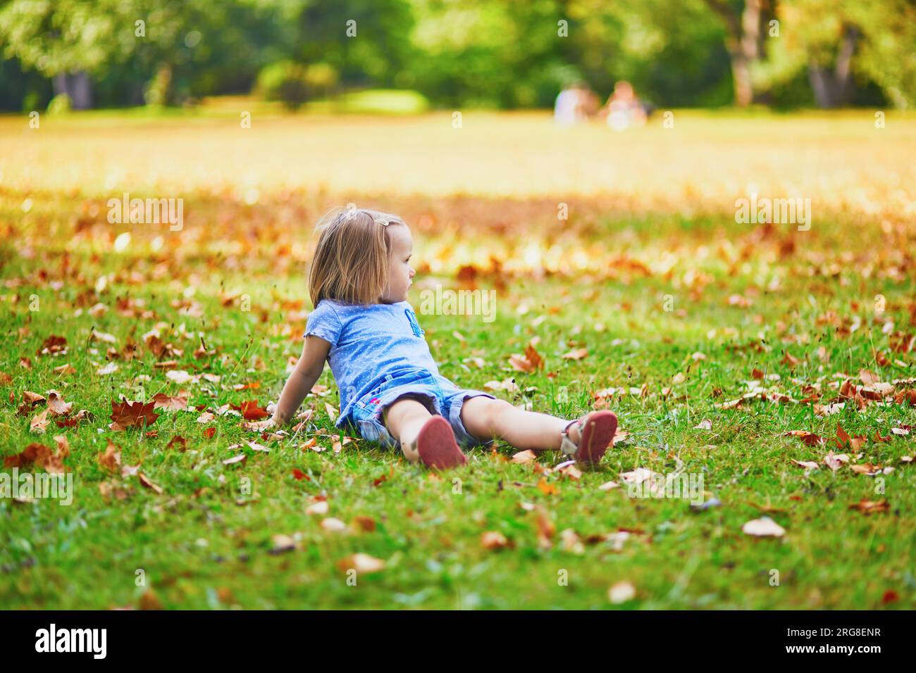 Unhappy and emotional toddler girl sitting on the ground in park ...