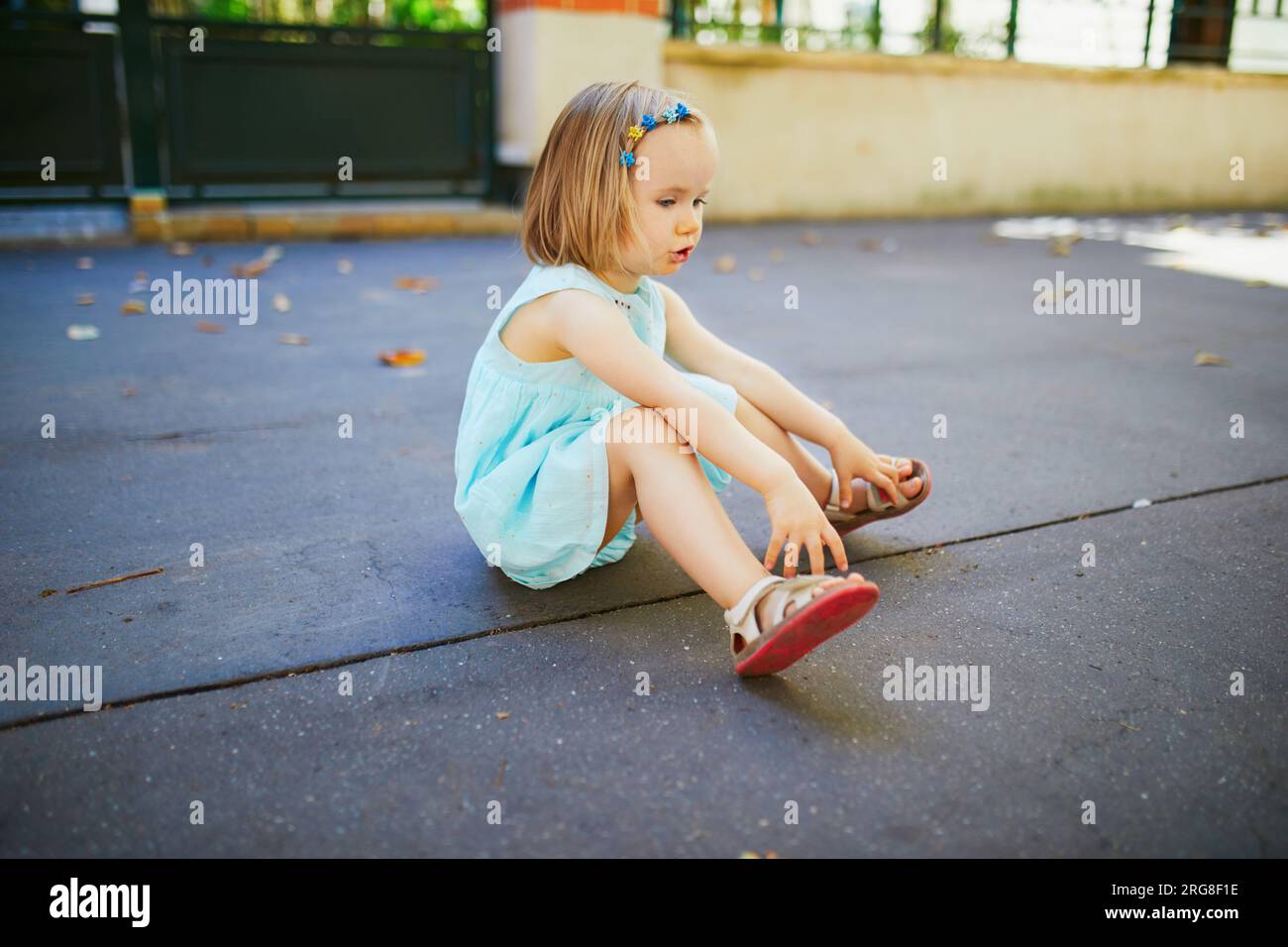 Unhappy and emotional toddler girl sitting on the floor outdoors ...