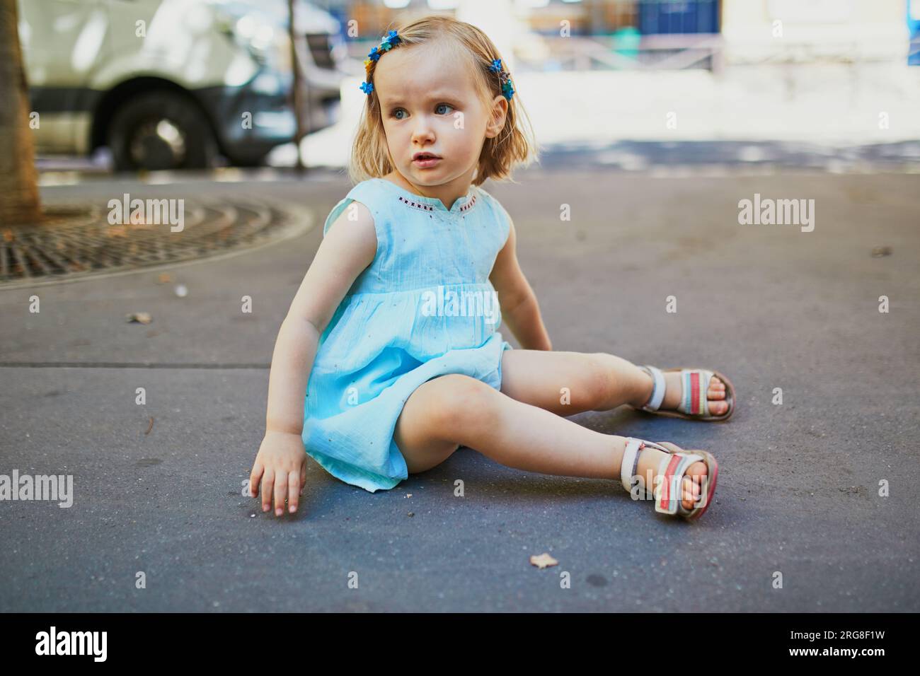 Unhappy and emotional toddler girl sitting on the floor outdoors ...