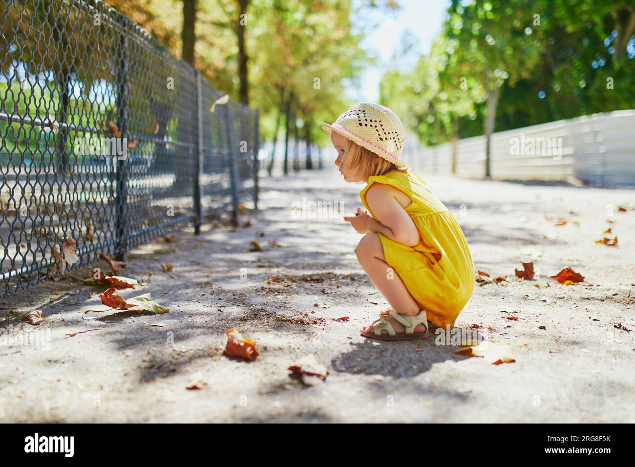 Cute little toddler girl squatting on her haunches on the playground on ...