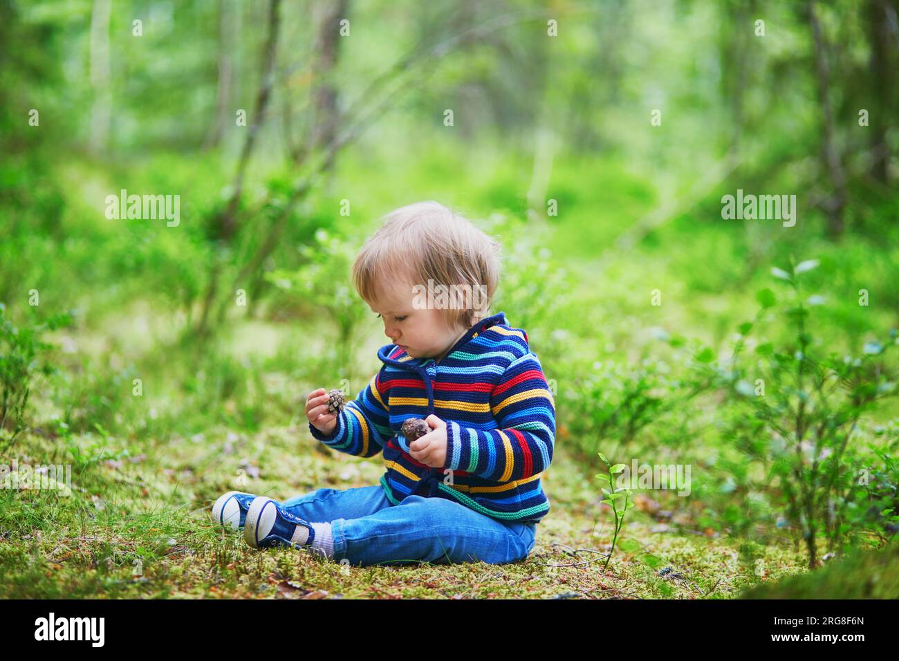Adorable baby girl in the forest, sitting on the ground and playing ...