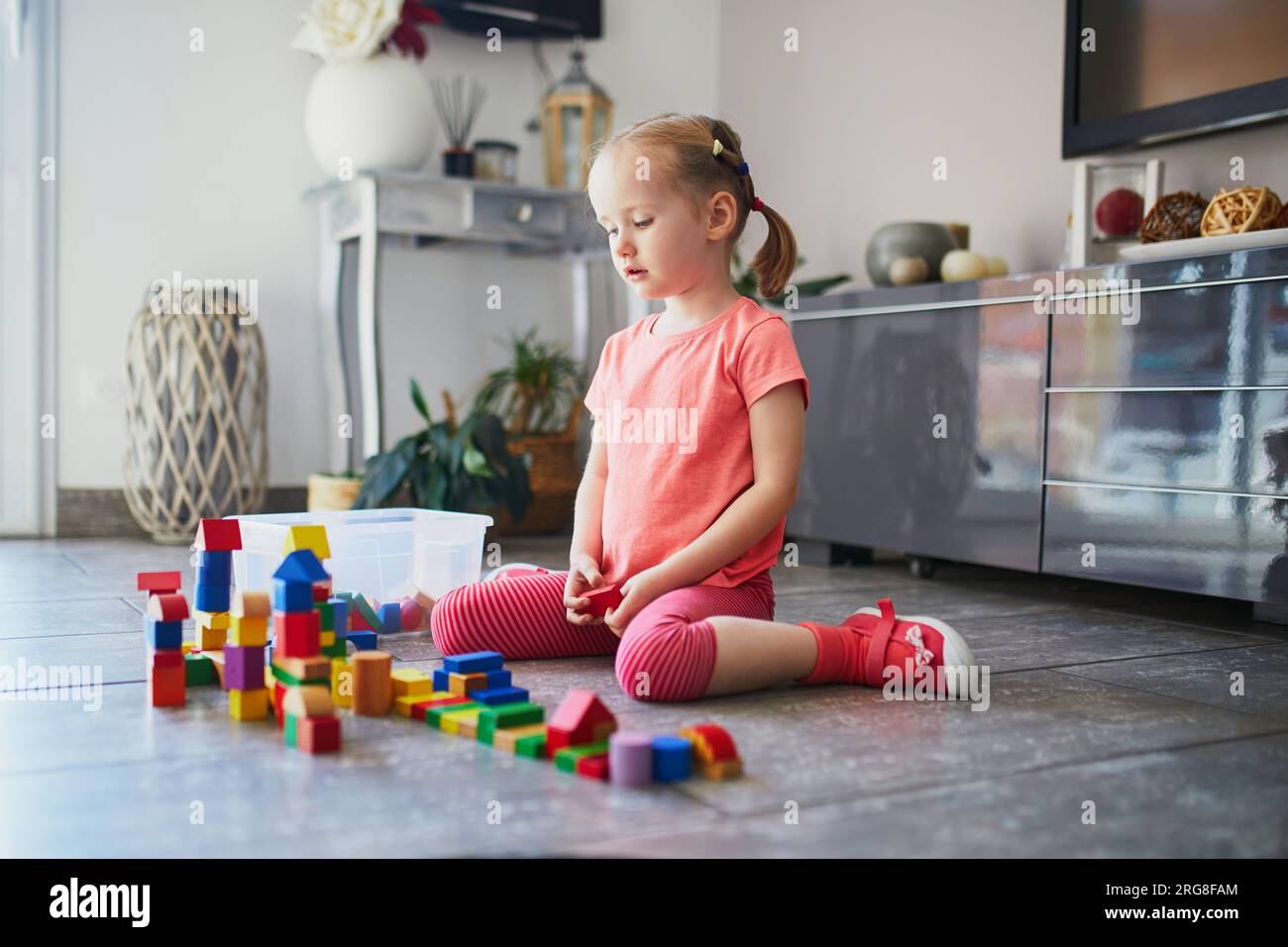 Adorable little girl playing with colorful plastic construction blocks ...