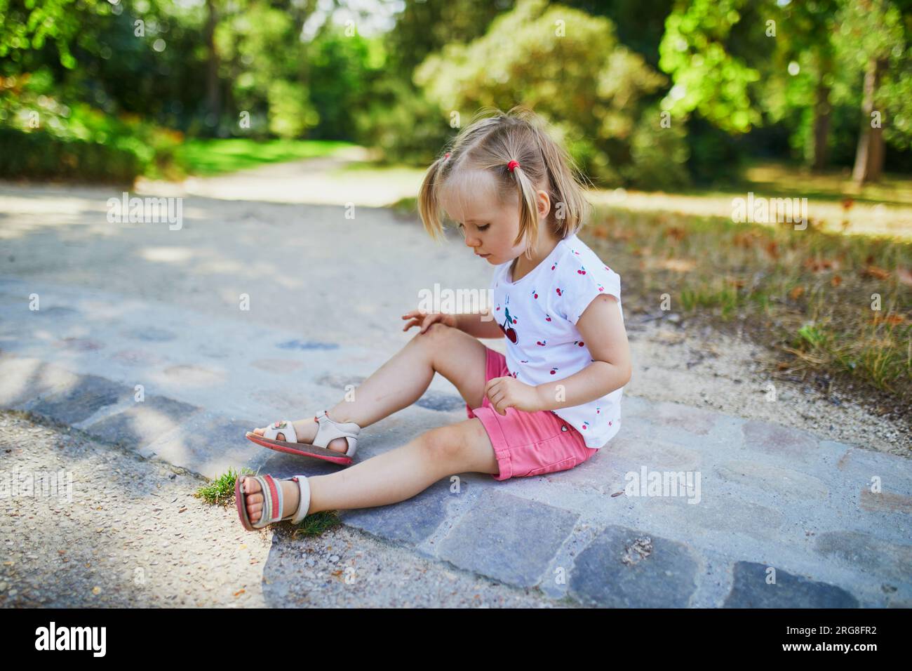 Cute little toddler girl sitting on the ground after falling at summer ...
