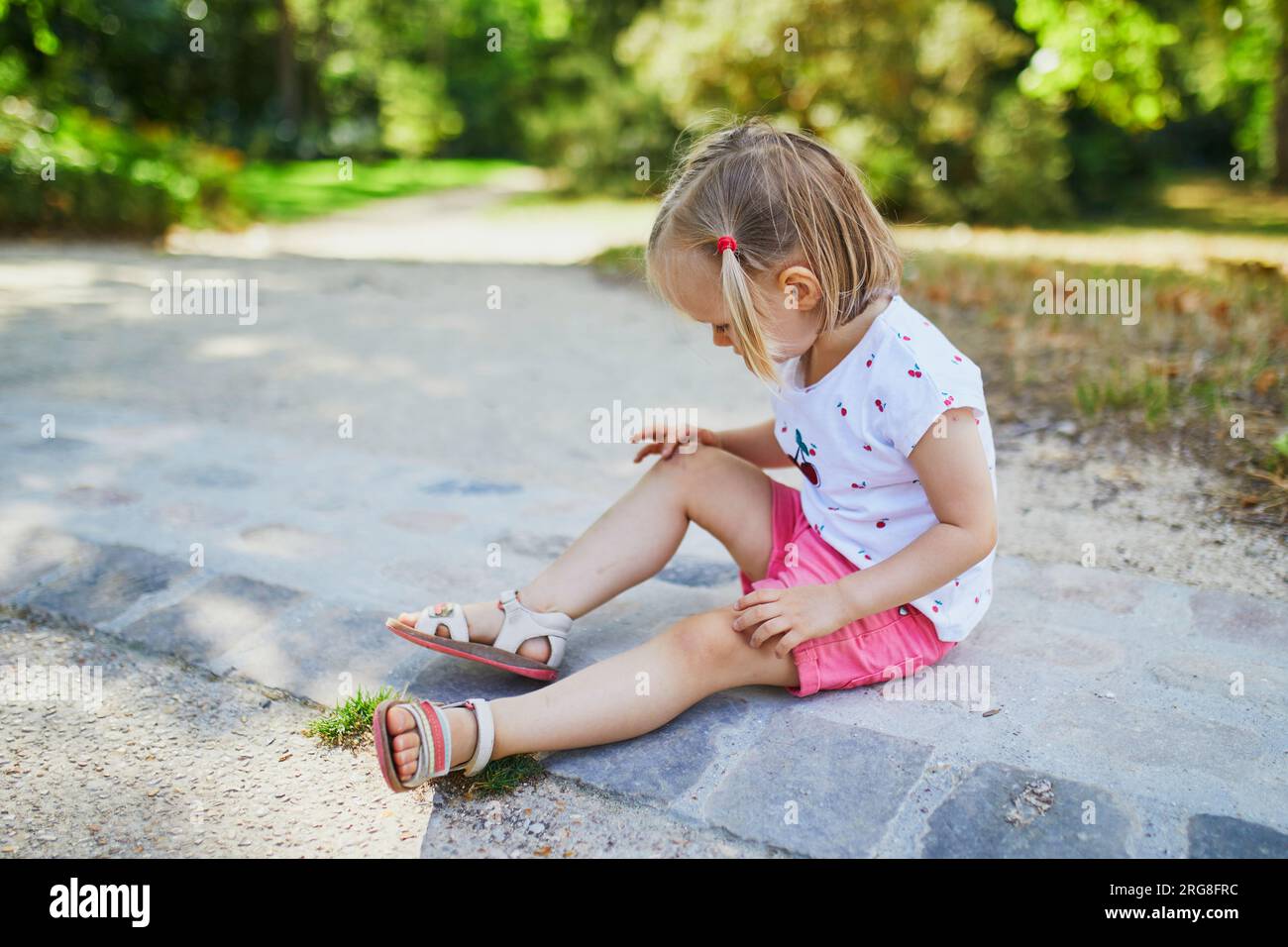Cute little toddler girl sitting on the ground after falling at summer ...