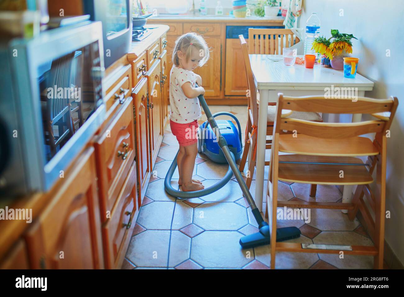 Adorable toddler girl using vacuum cleaner at home. Child helping ...