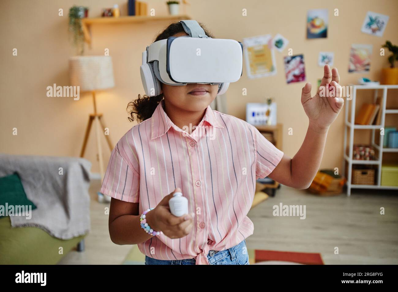 Cute AFrican American schoolgirl in VR headset playing virtual game ...