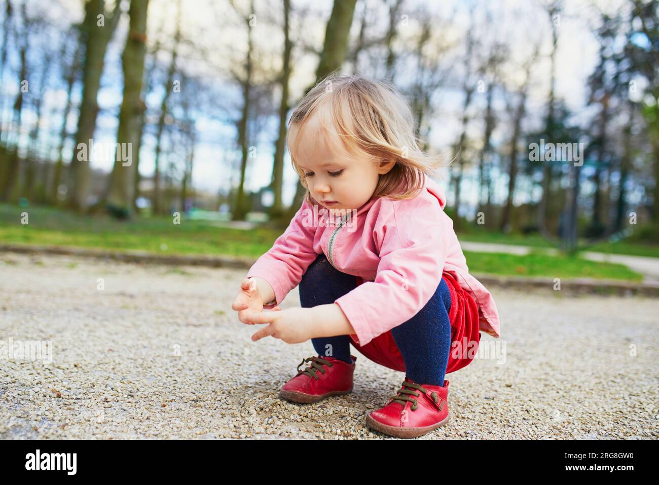 Adorable baby girl in park, sitting on hunkers and playing with little ...