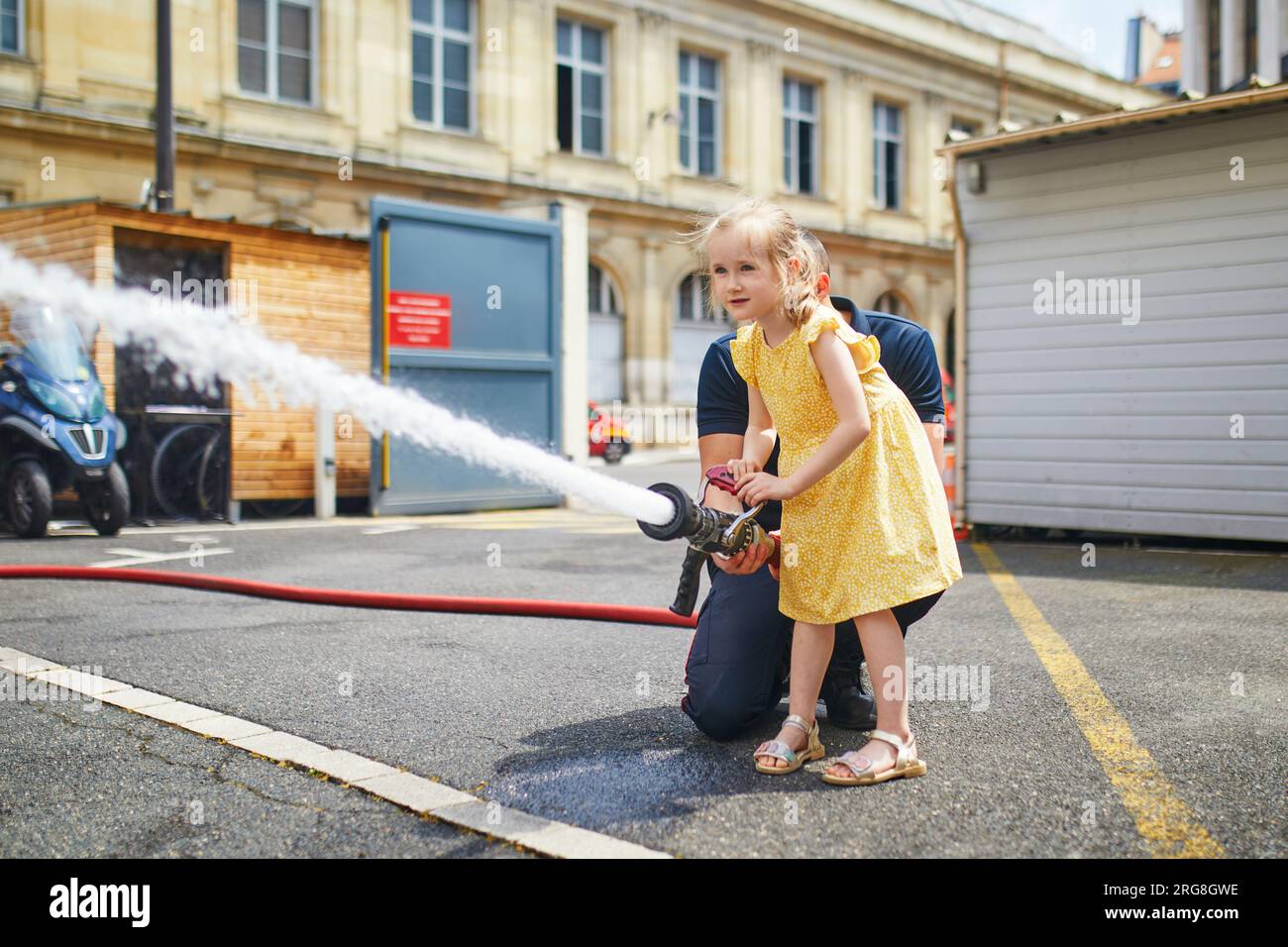 Adorable preschooler girl acting like a fireman holding firehose nozzle ...
