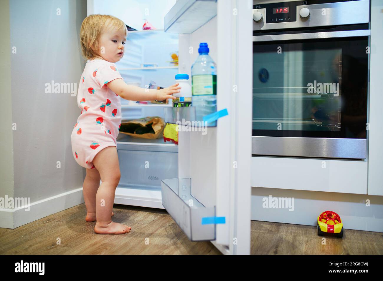 Adorable toddler girl at home, opening the fridge and selecting food ...