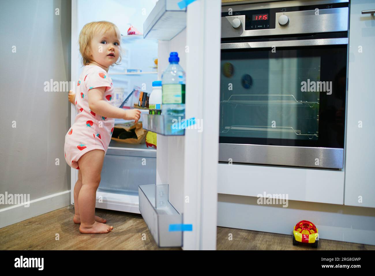 Adorable toddler girl at home, opening the fridge and selecting food ...