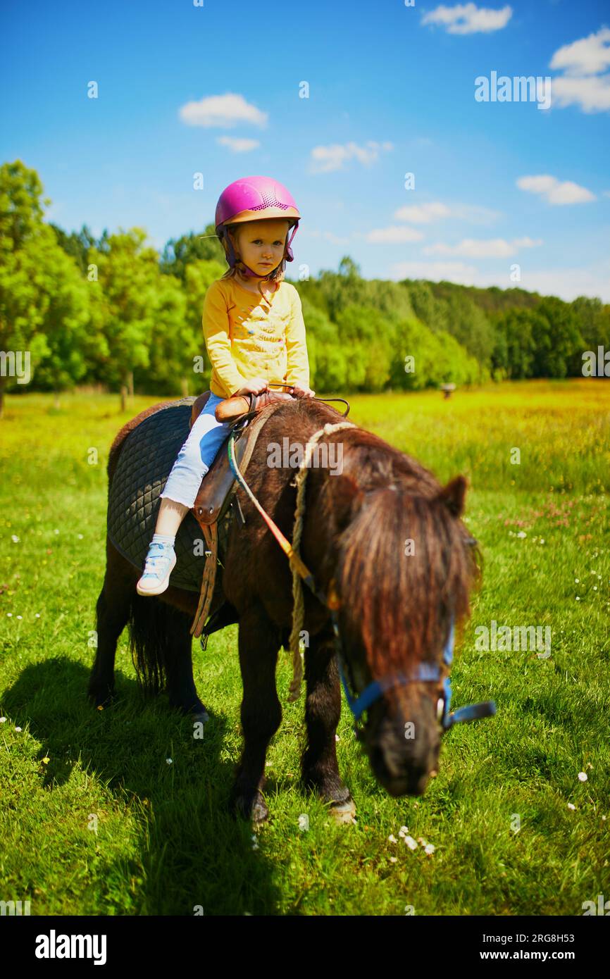 Adorable three years old girl riding a pony. Little child practicing ...