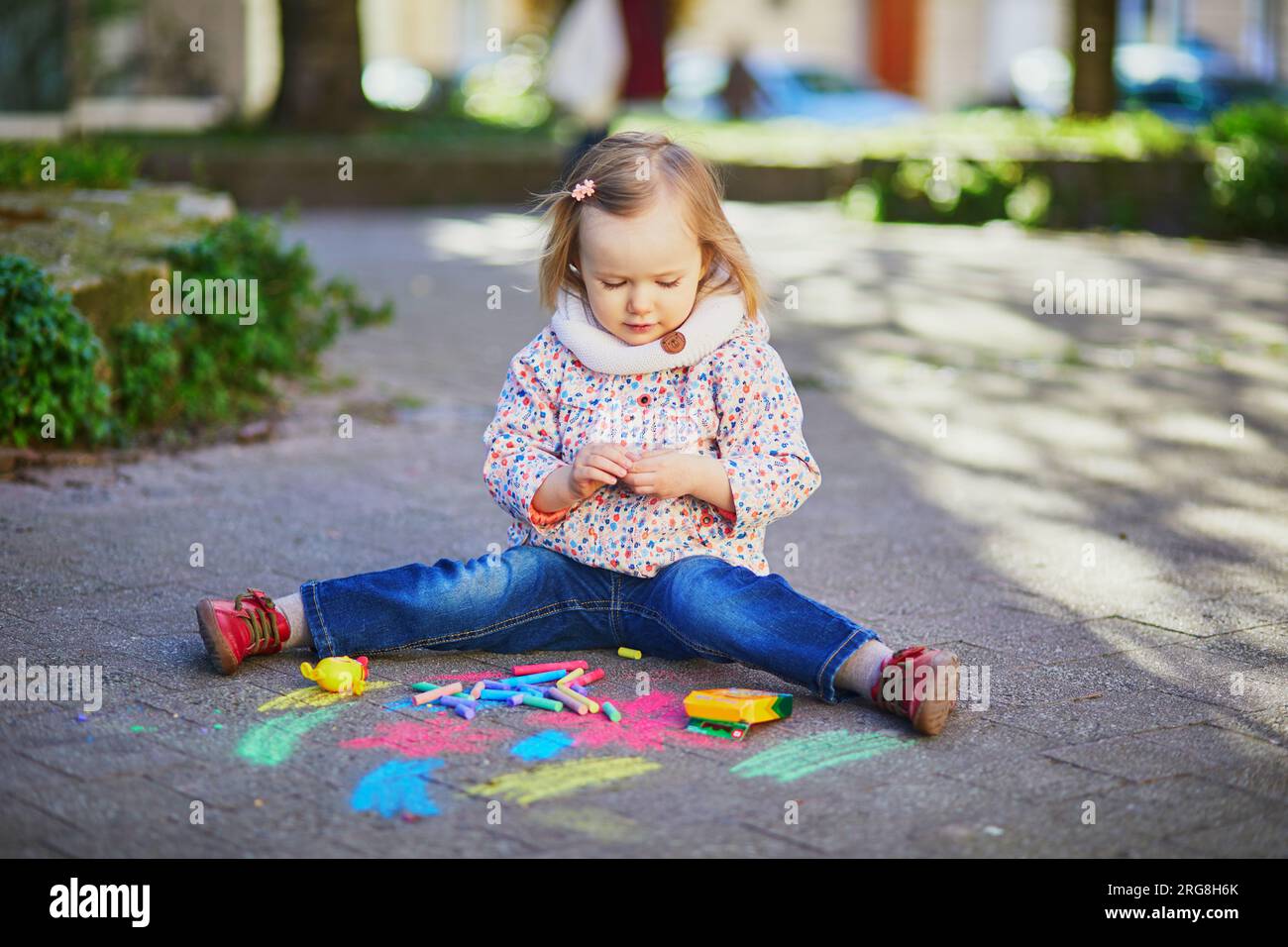 Adorable toddler girl drawing with colorful chalks on asphalt. Outdoor ...