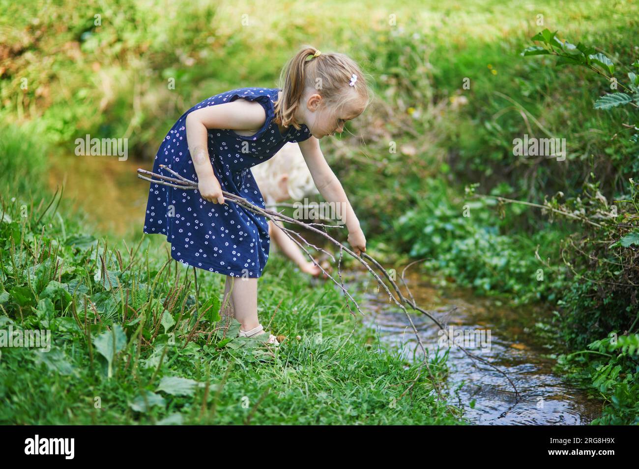 Preschooler girl playing with a twig like with fishing rod. Role games ...