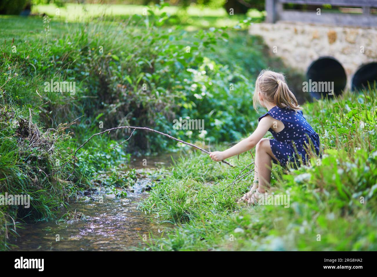 Preschooler girl playing with a twig like with fishing rod. Role games ...