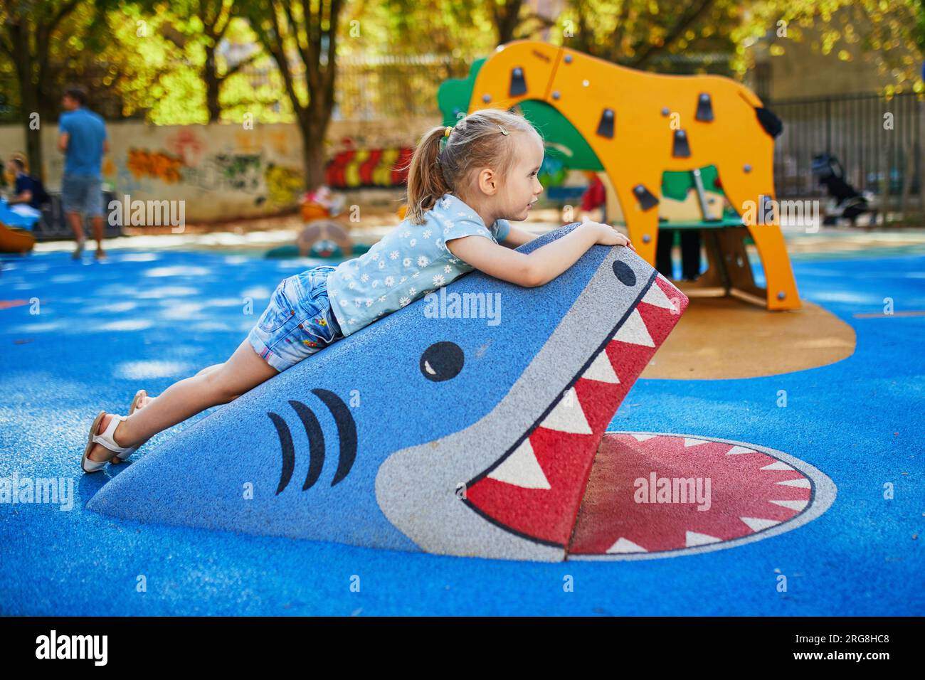 Adorable preschooler girl playing with giant shark on a playground ...
