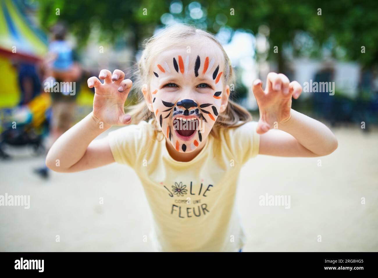 Little preschooler girl with tiger face painting outdoors. Children ...