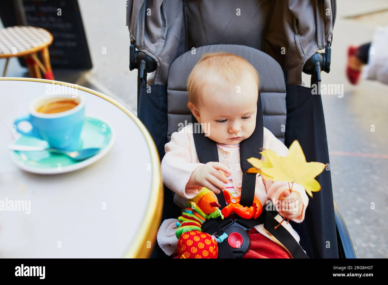 Little baby girl in pushchair in Parisian outdoor cafe on a fall day ...