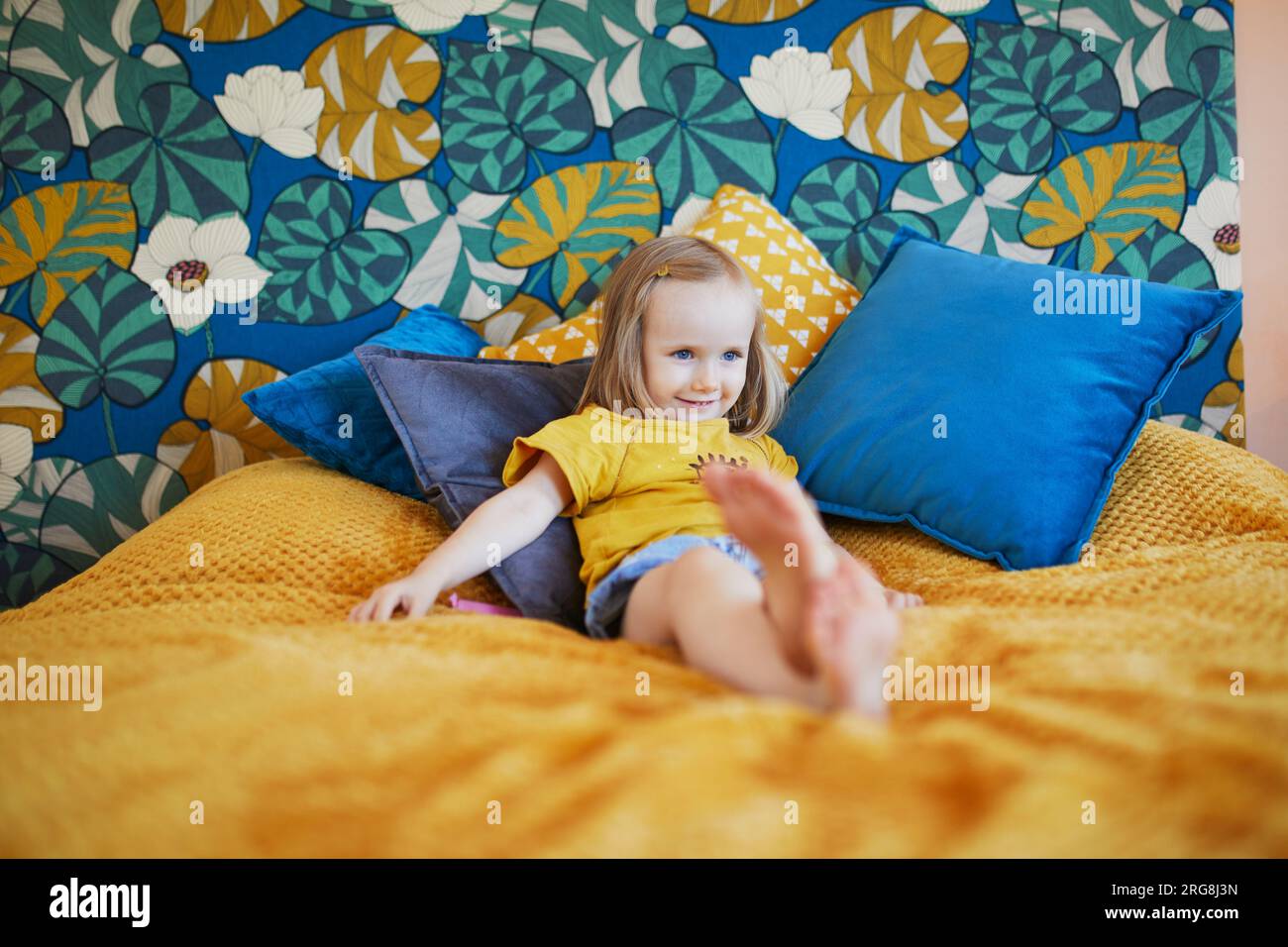 Adorable playful little girl sitting on bed in nicely decorated bedroom ...