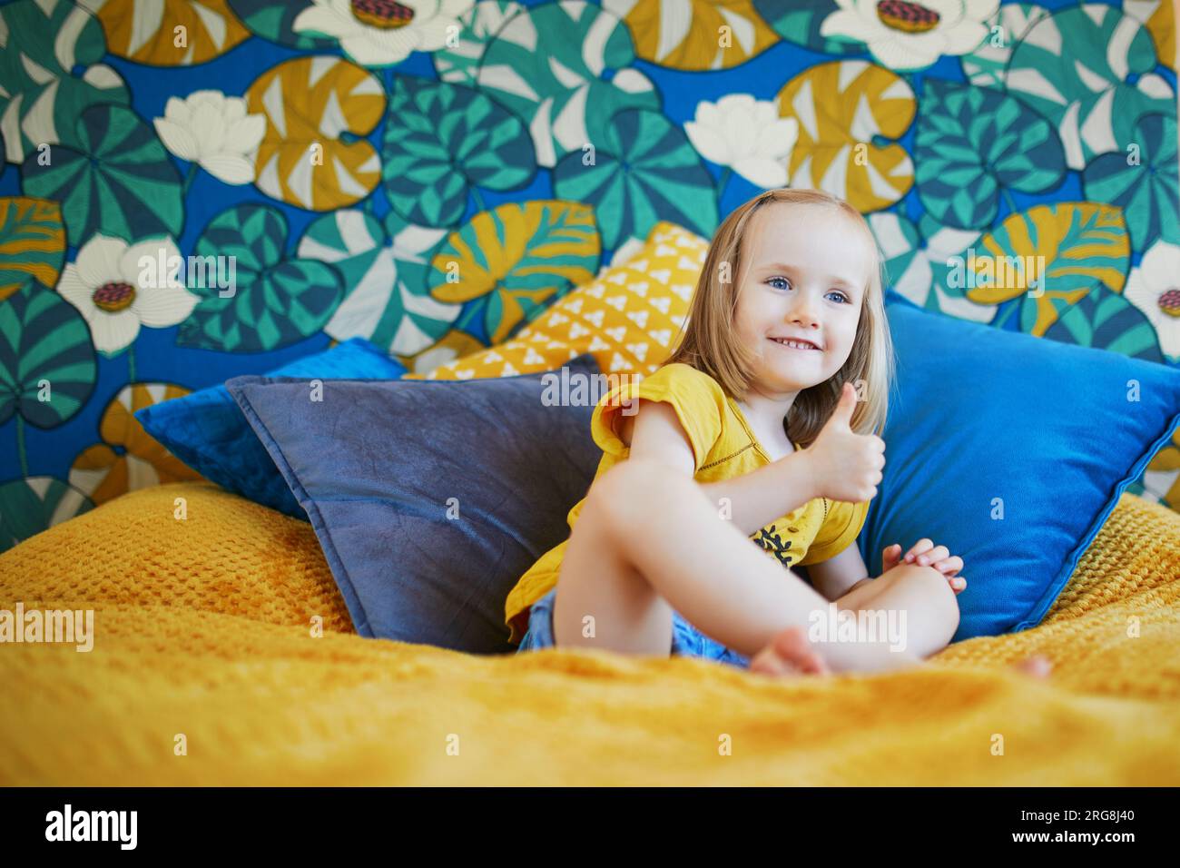 Adorable playful little girl sitting on bed in nicely decorated bedroom ...