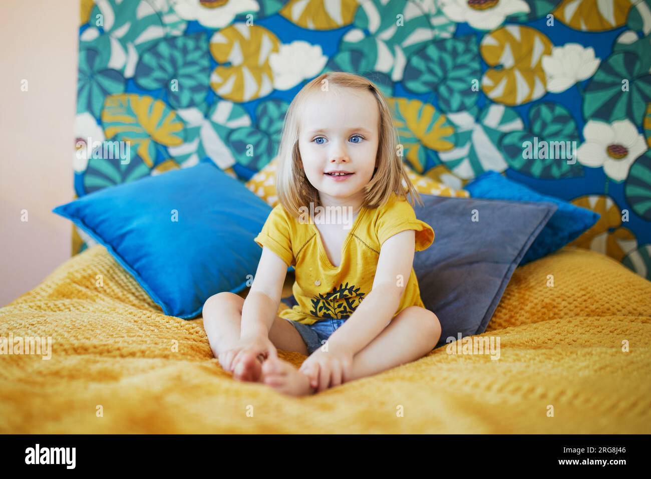Adorable playful little girl sitting on bed in nicely decorated bedroom ...