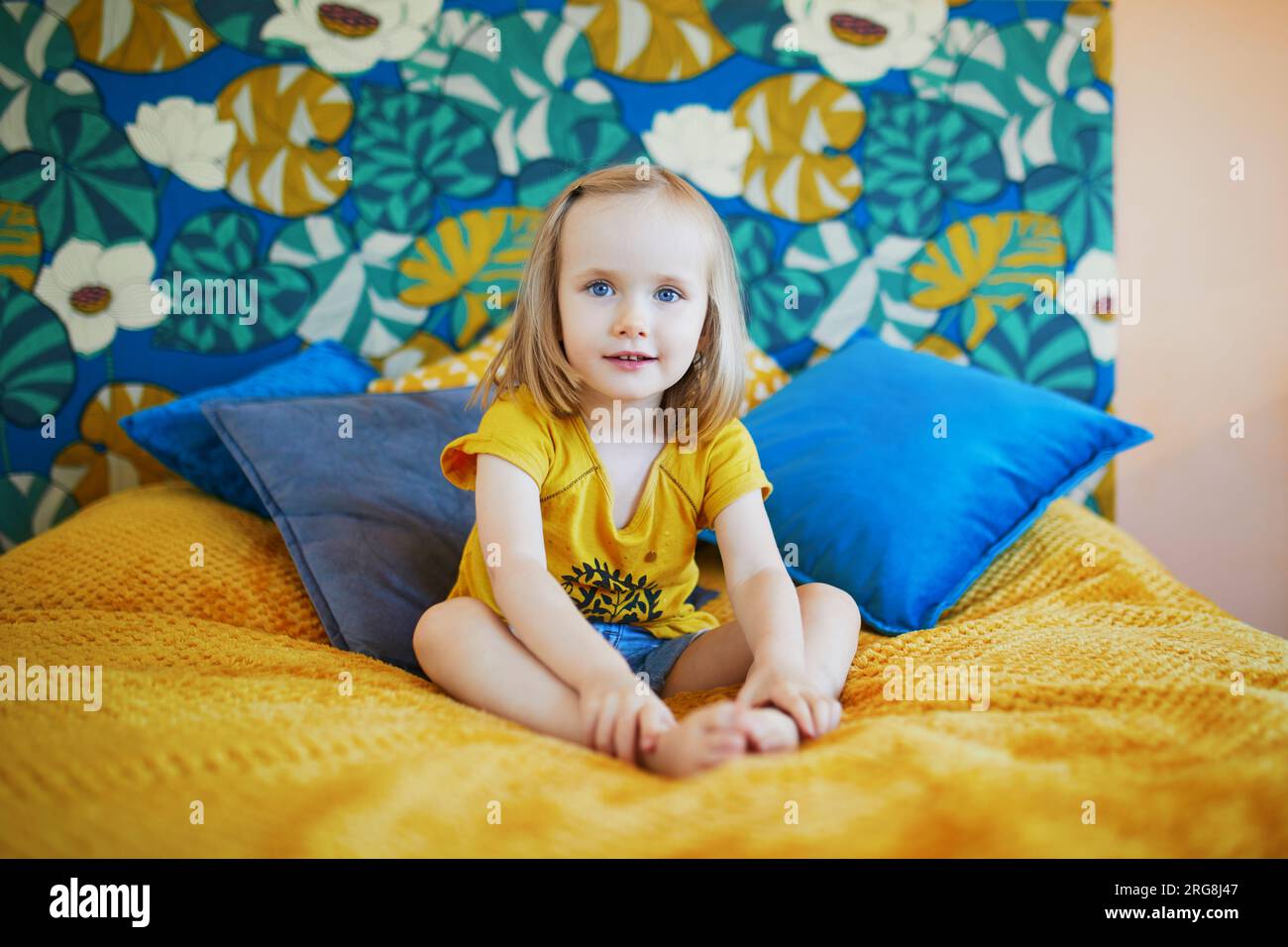 Adorable playful little girl sitting on bed in nicely decorated bedroom ...