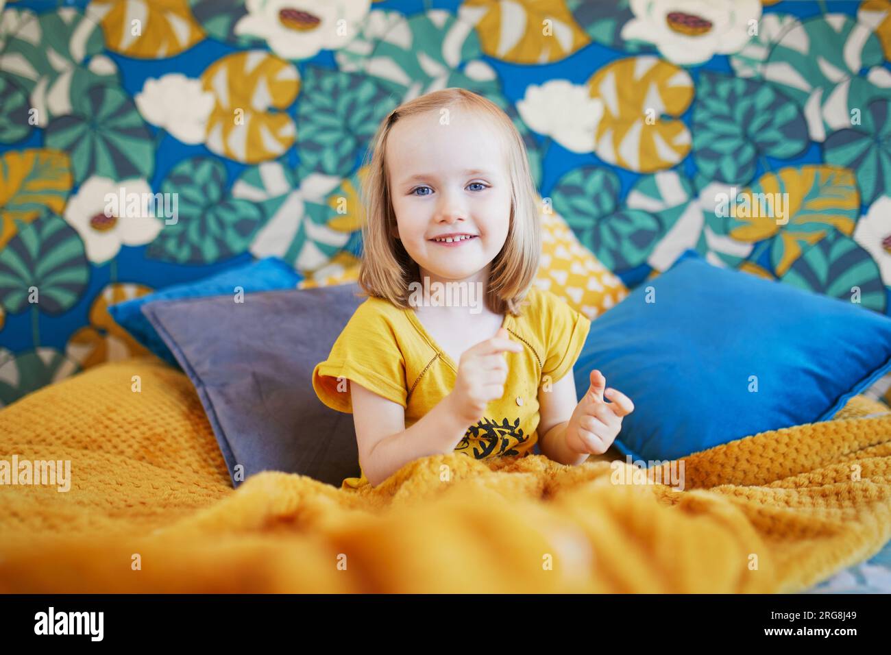 Adorable playful little girl sitting on bed in nicely decorated bedroom ...