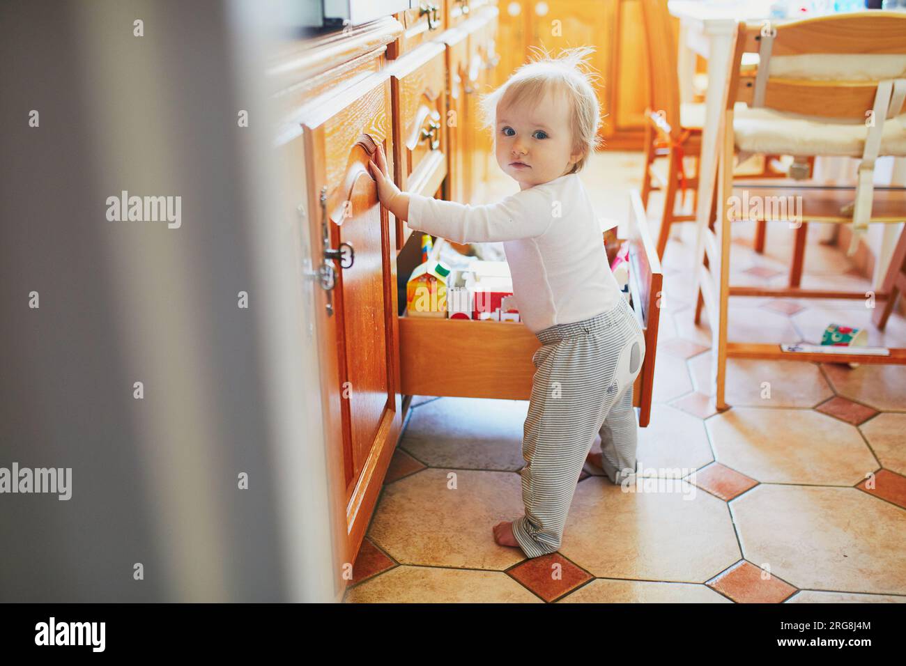 Adorable toddler girl at home, opening the drawer in the kitchen and ...