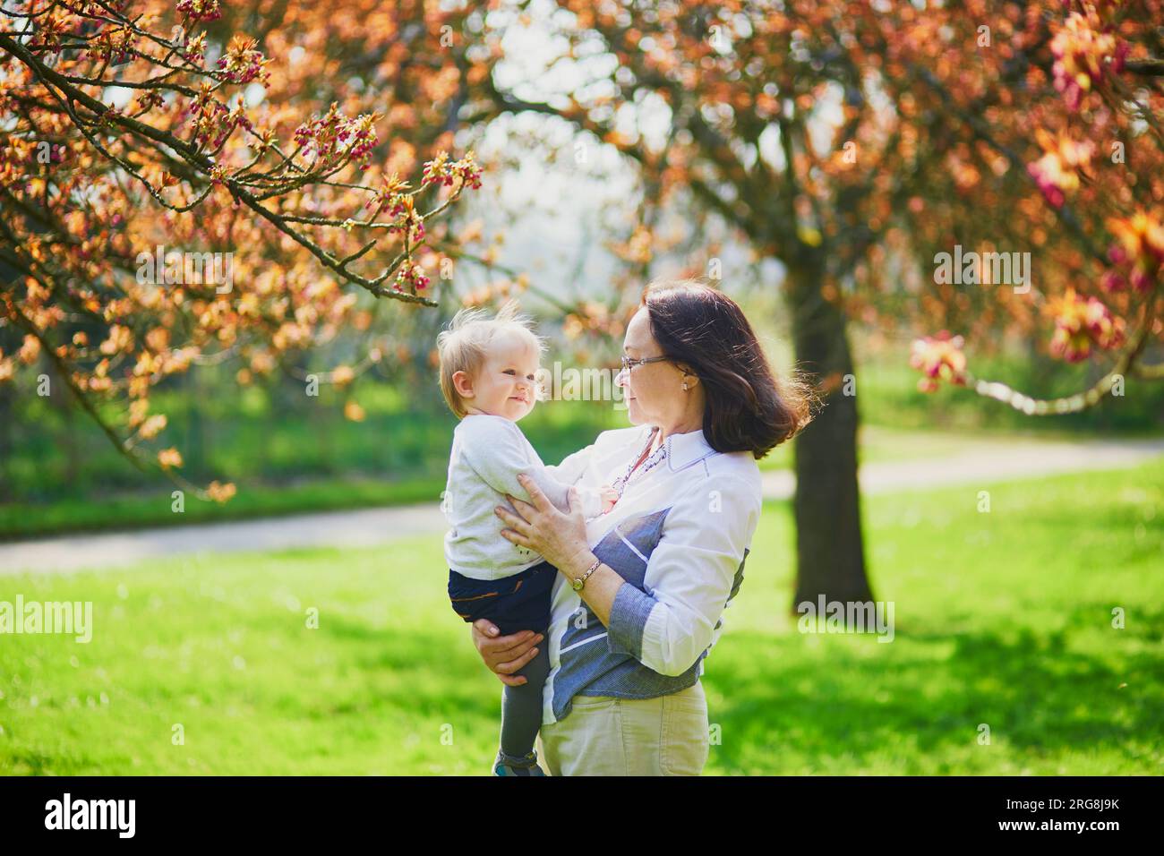 Middle aged woman holding 1 year old baby girl in park on a spring day ...