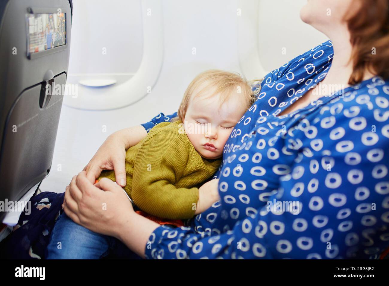 Woman with little girl travelling by plane. Mother holding her sleeping ...