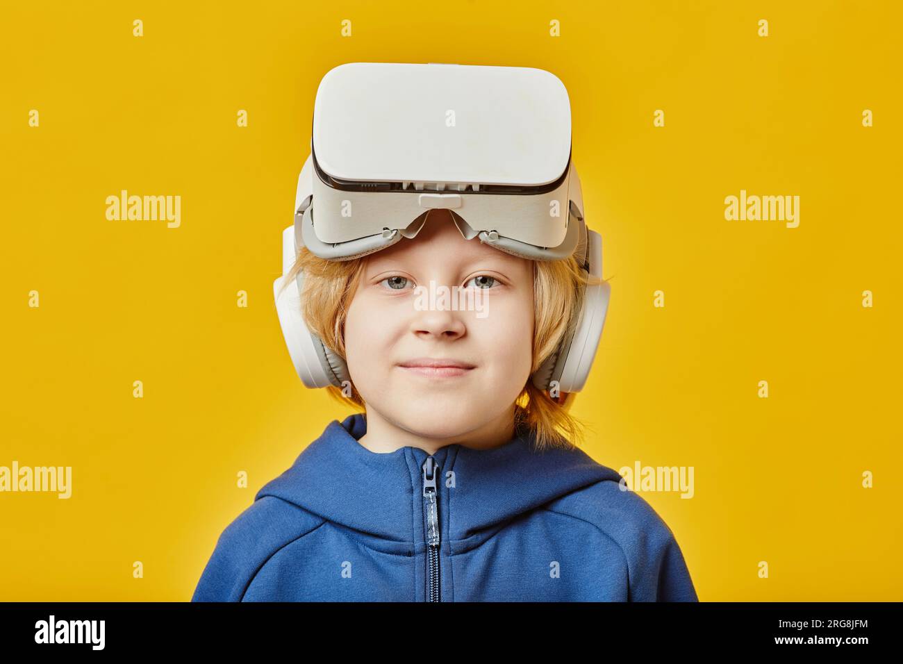 Cute blond boy with VR headset on forehead looking at camera after ...