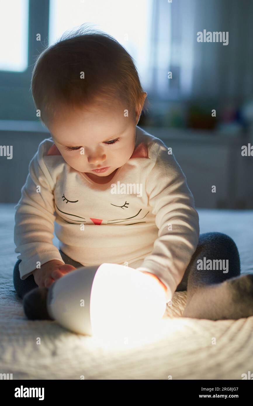 Adorable baby girl playing with bedside lamp in nursery. Happy kid ...