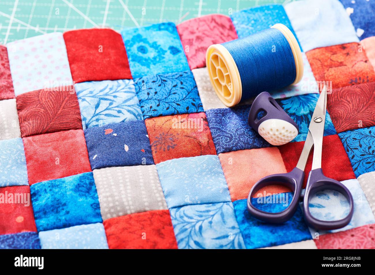 Scissors, thread and thimble lying on blue and red square pieces of ...