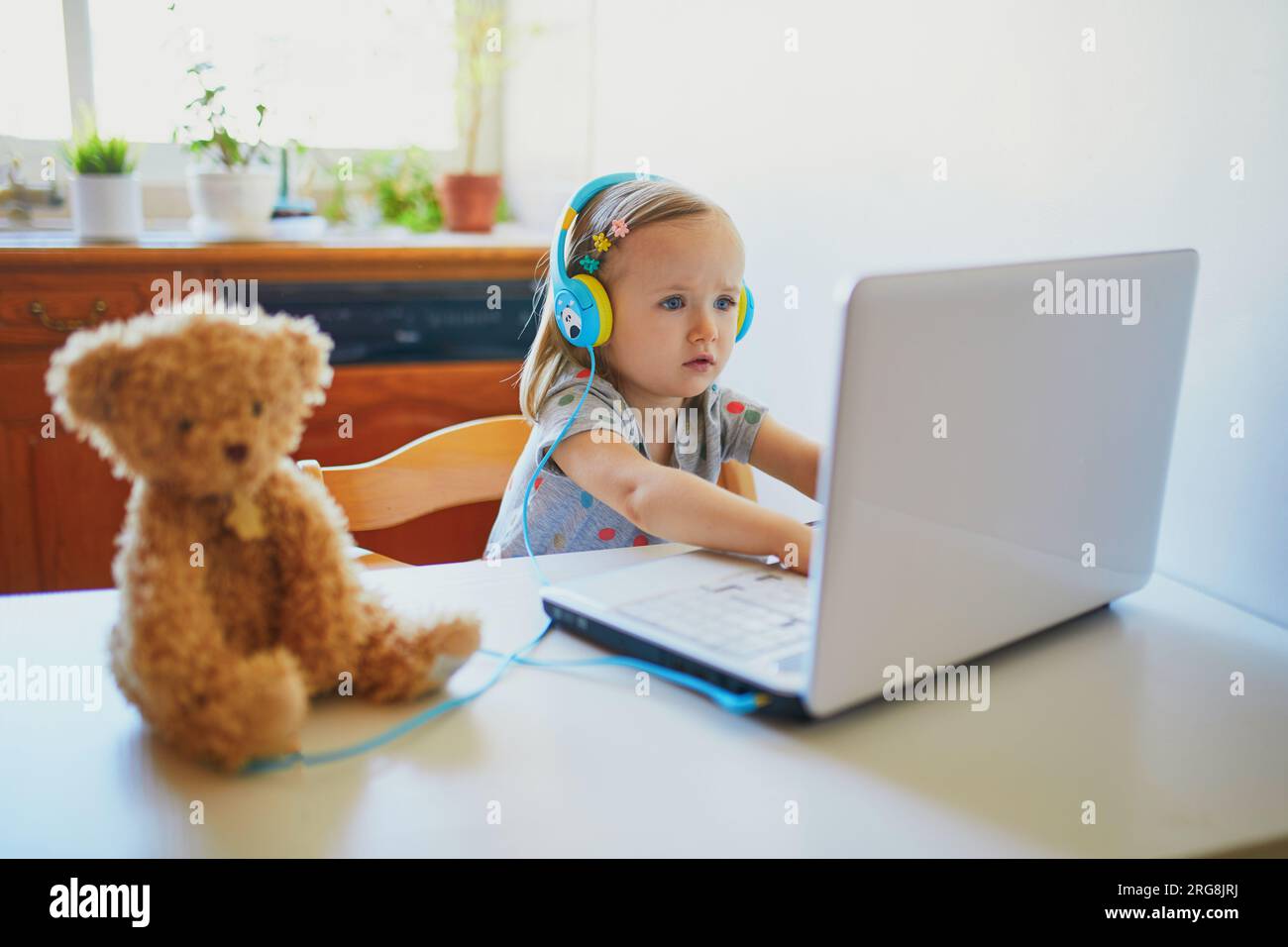 Toddler girl wearing eraphones with laptop. Kid using computer to ...
