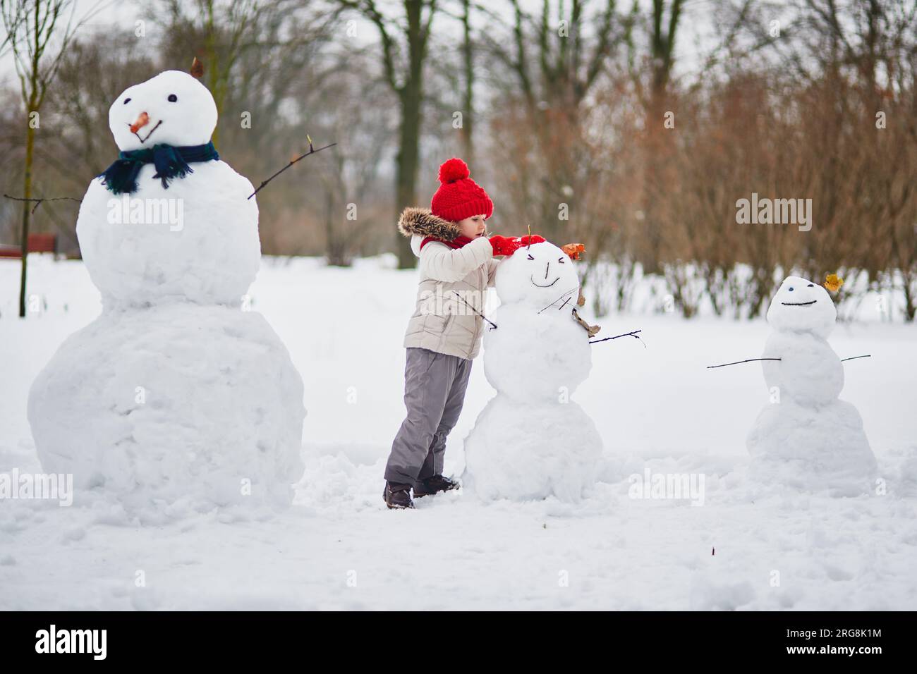 Adorable preschooler girl building a snowman on a day with heavy ...