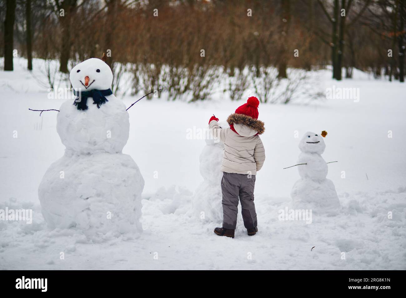 Adorable preschooler girl building a snowman on a day with heavy ...
