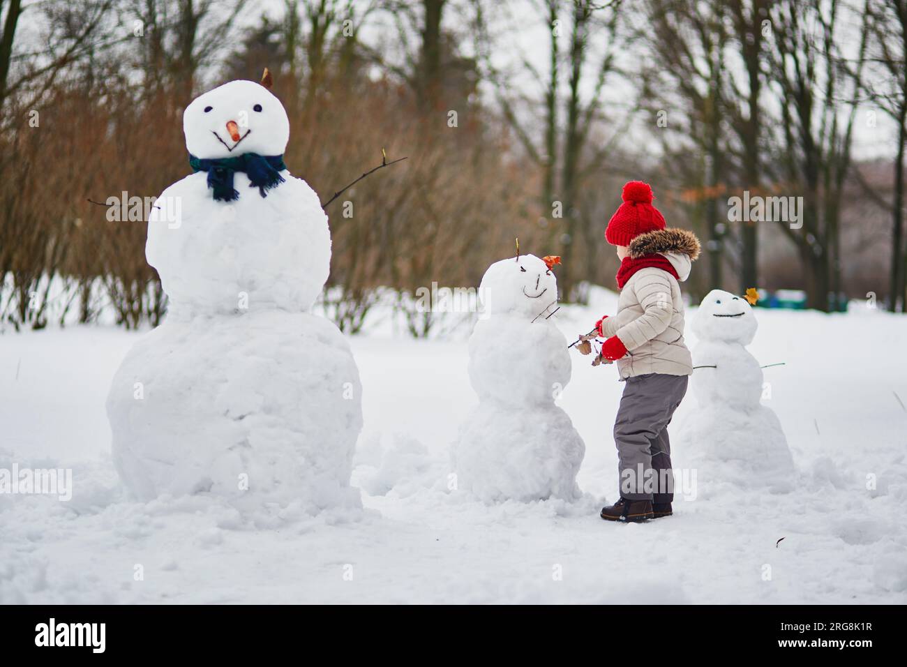 Adorable preschooler girl building a snowman on a day with heavy ...