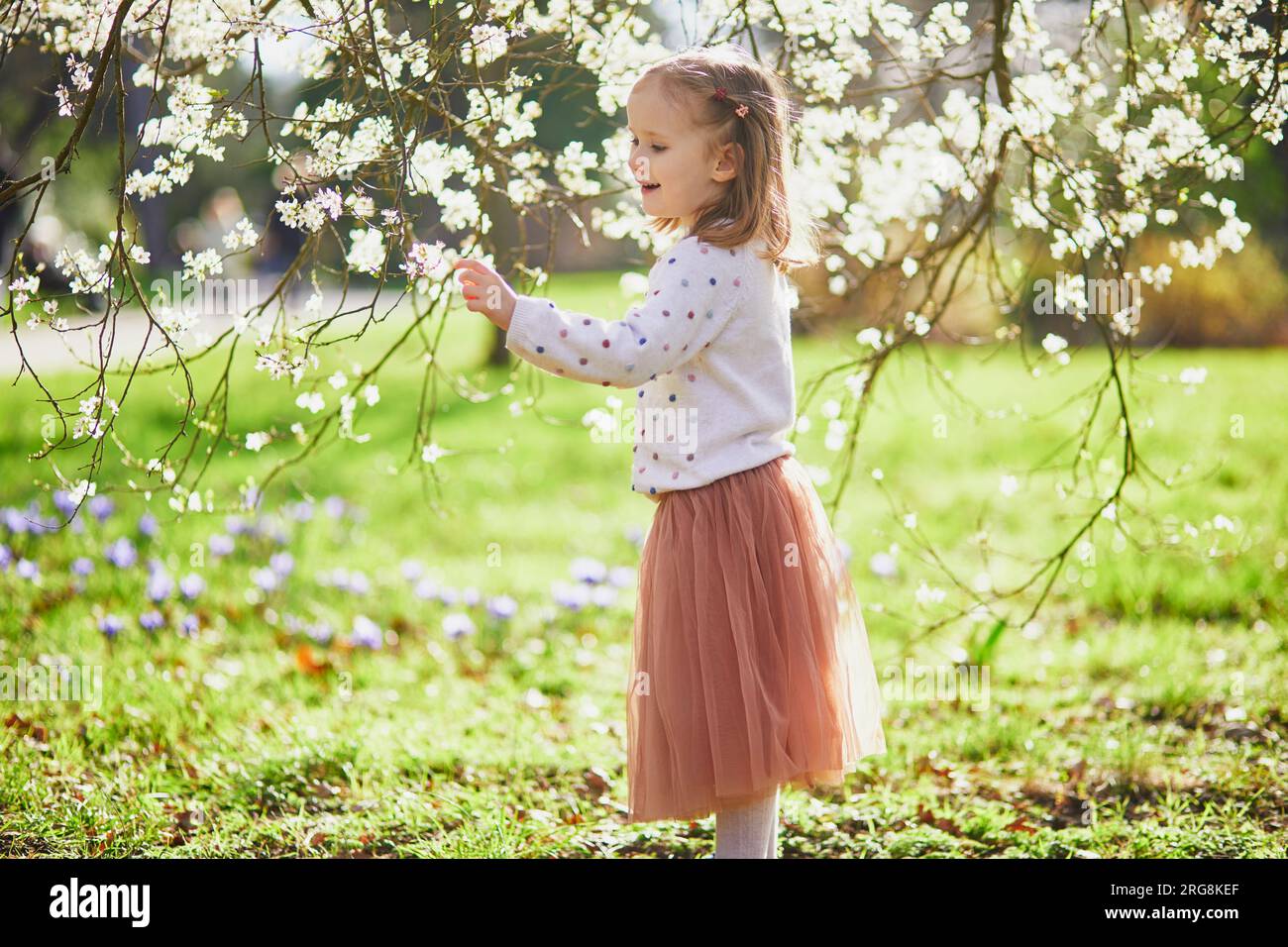 Adorable little girl enjoying nice and sunny spring day near apple tree ...