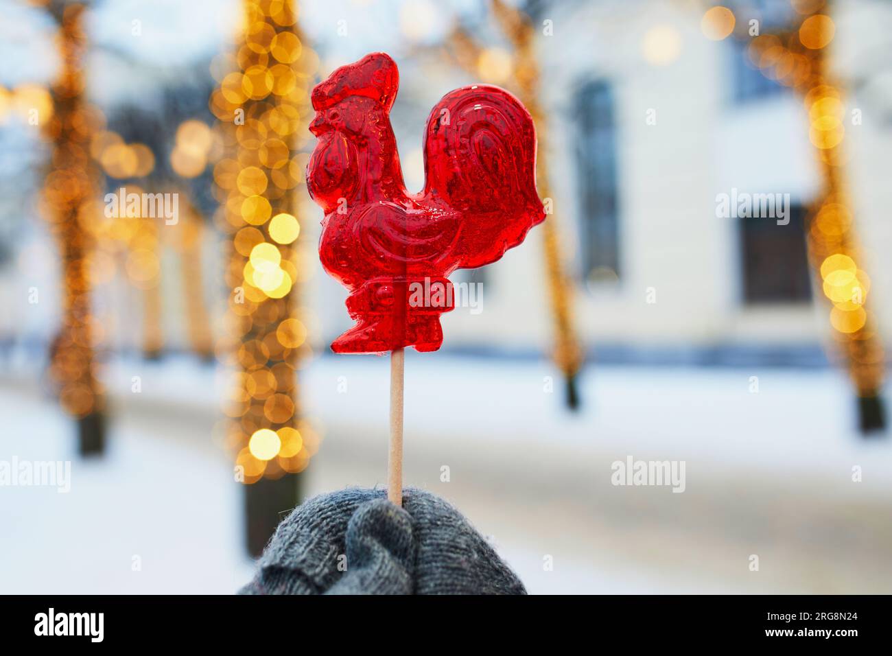 Hand in grey mitten holding rooster-shaped lollipop on a Christmas ...