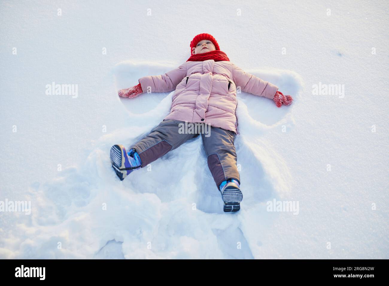 Adorable preschooler girl making snow angel in beautiful winter park on ...