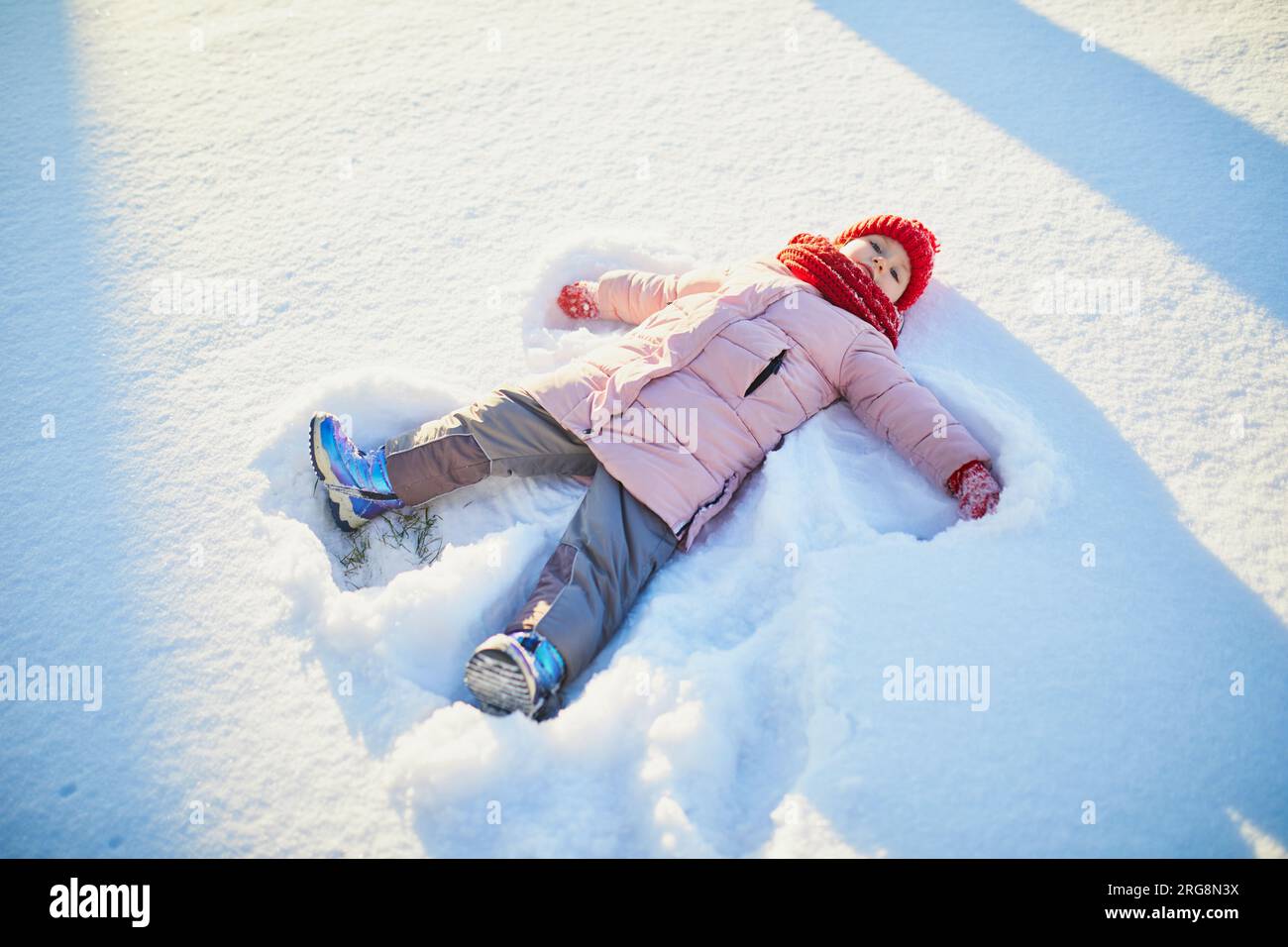 Adorable preschooler girl making snow angel in beautiful winter park on ...